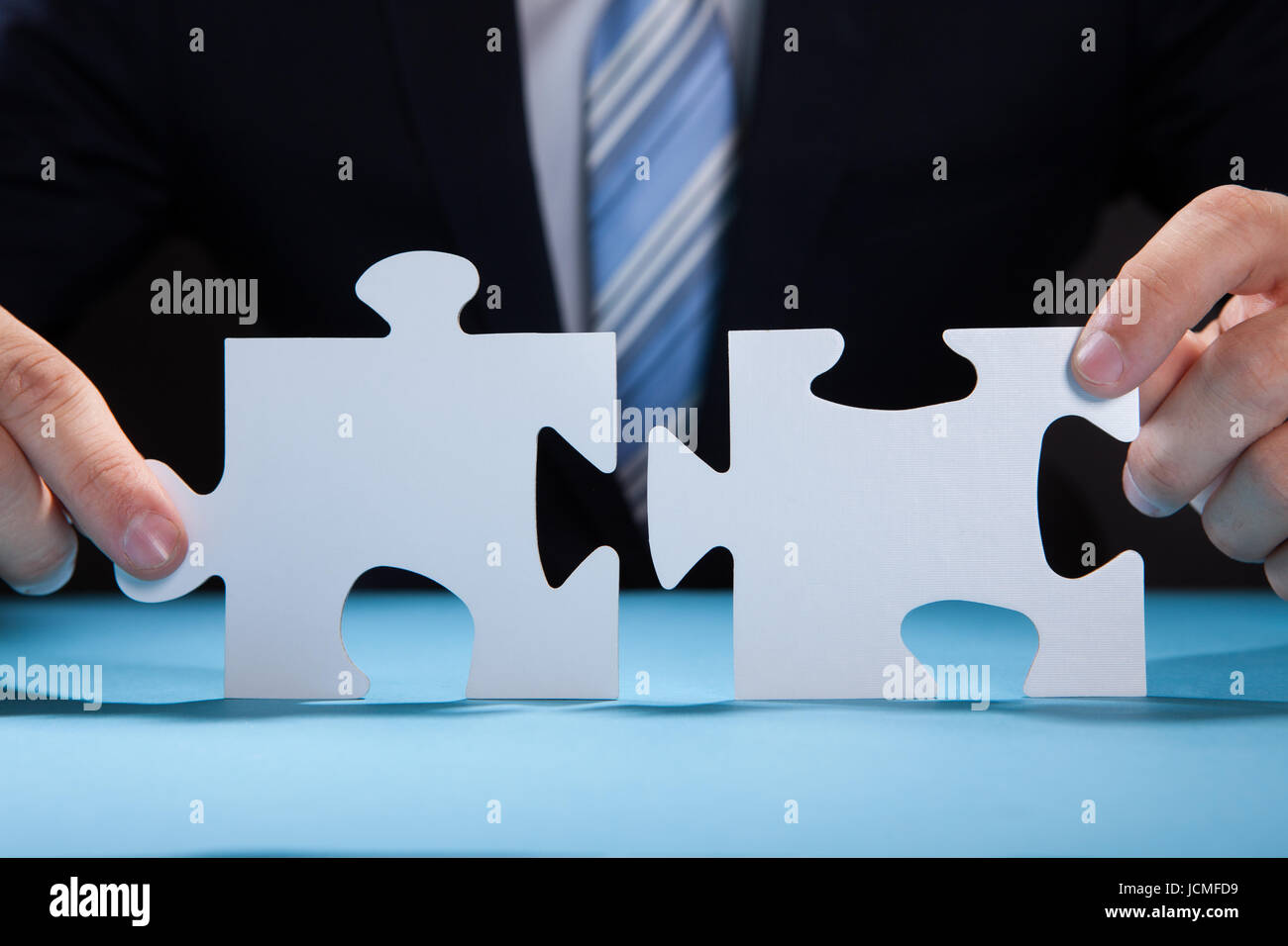 Closeup of businessman joining puzzle pieces at desk Stock Photo - Alamy