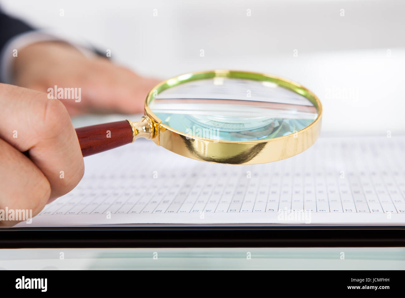 Cropped image of businessman examining audit with magnifying glass at ...