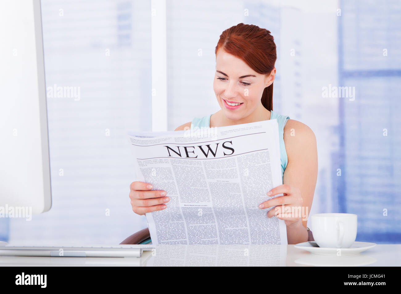 Happy young woman reading newspaper at computer desk Stock Photo - Alamy