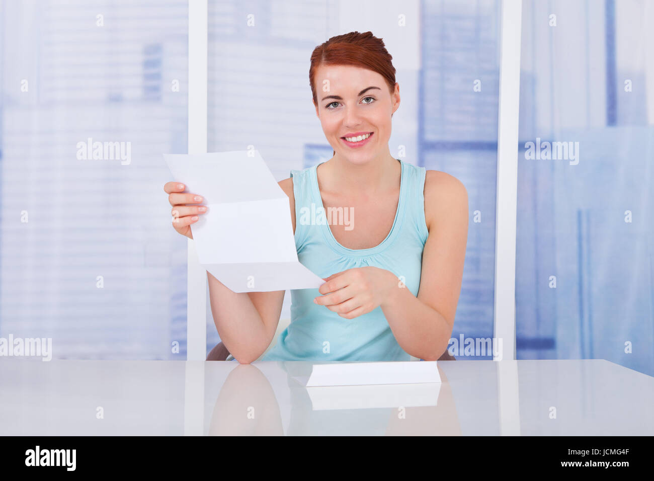 Portrait of happy young woman holding document at desk Stock Photo - Alamy