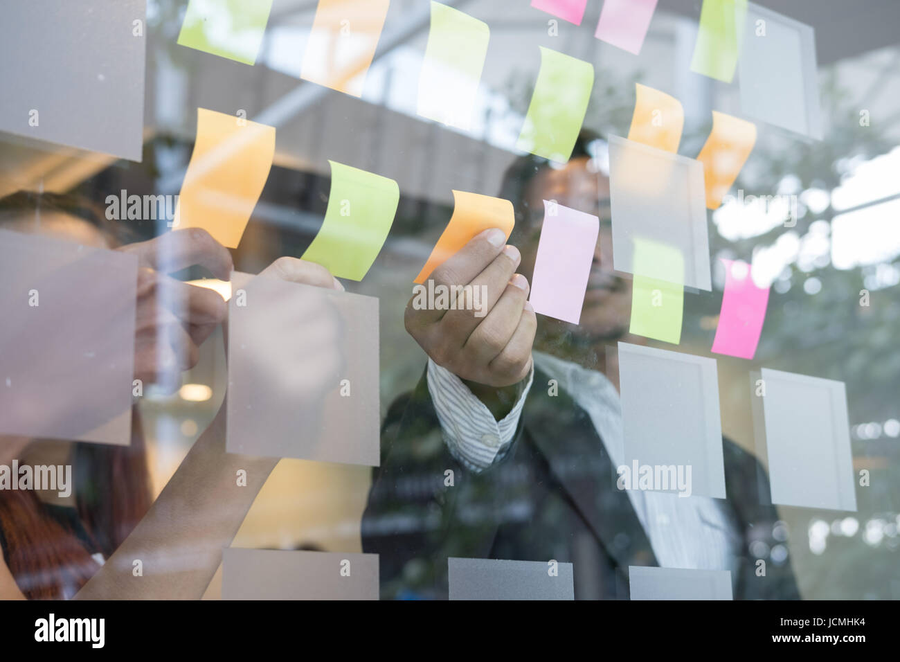 Business team look at the adhesive notes on glass wall in meeting room ...