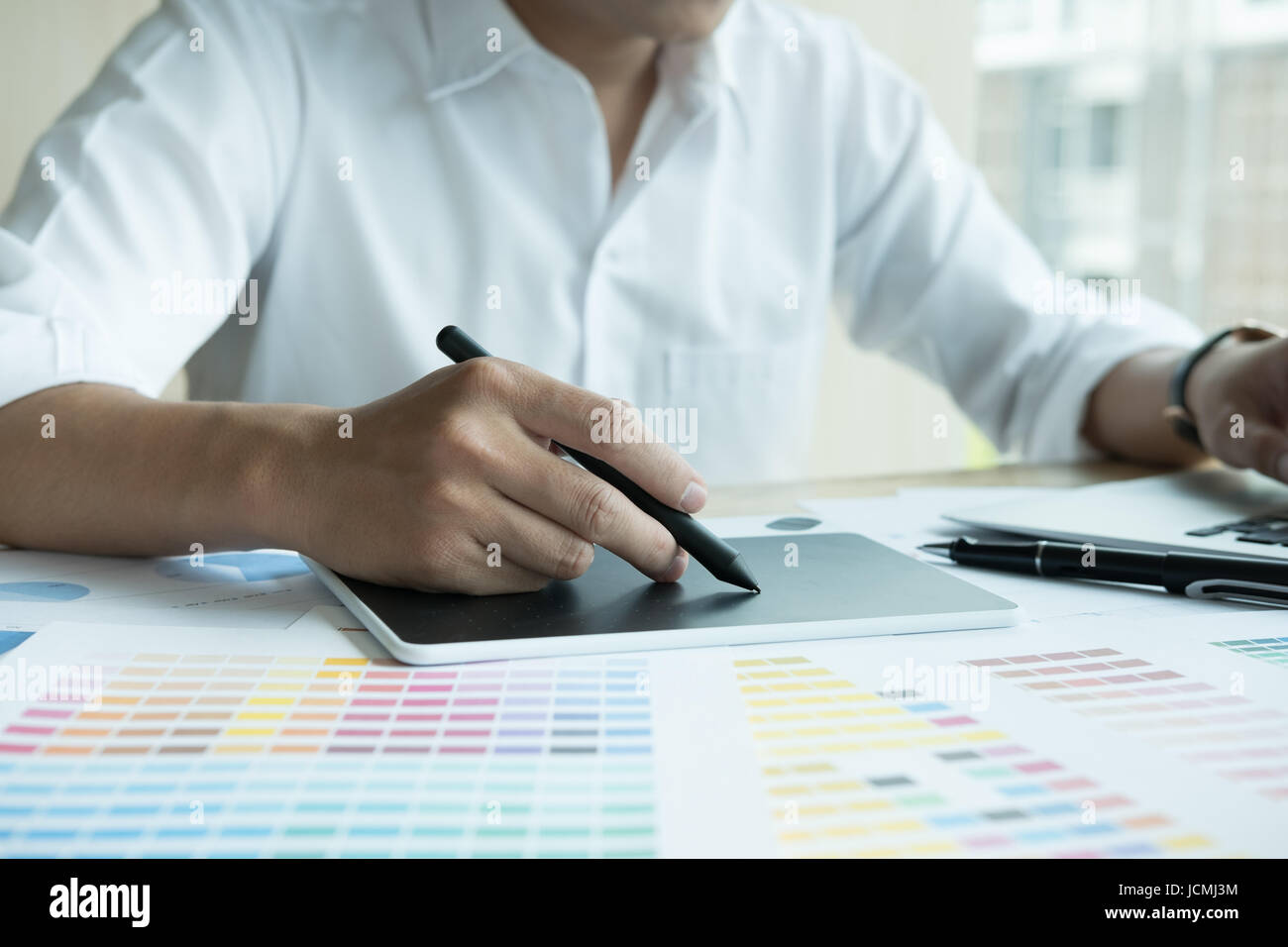 young male graphic designer working with computer and color swatch ...