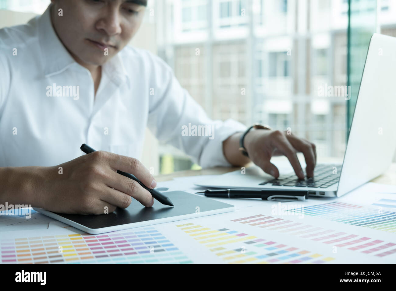young male graphic designer working with computer and color swatch ...