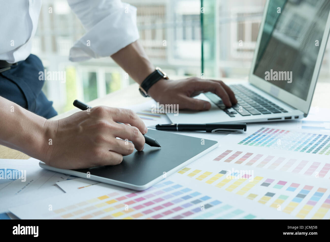 young male graphic designer working with computer and color swatch ...
