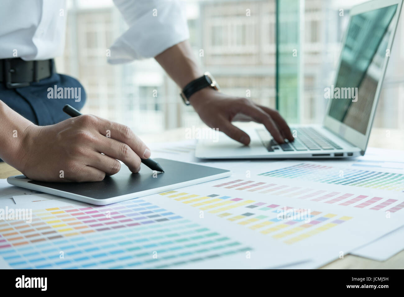 young male graphic designer working with computer and color swatch ...