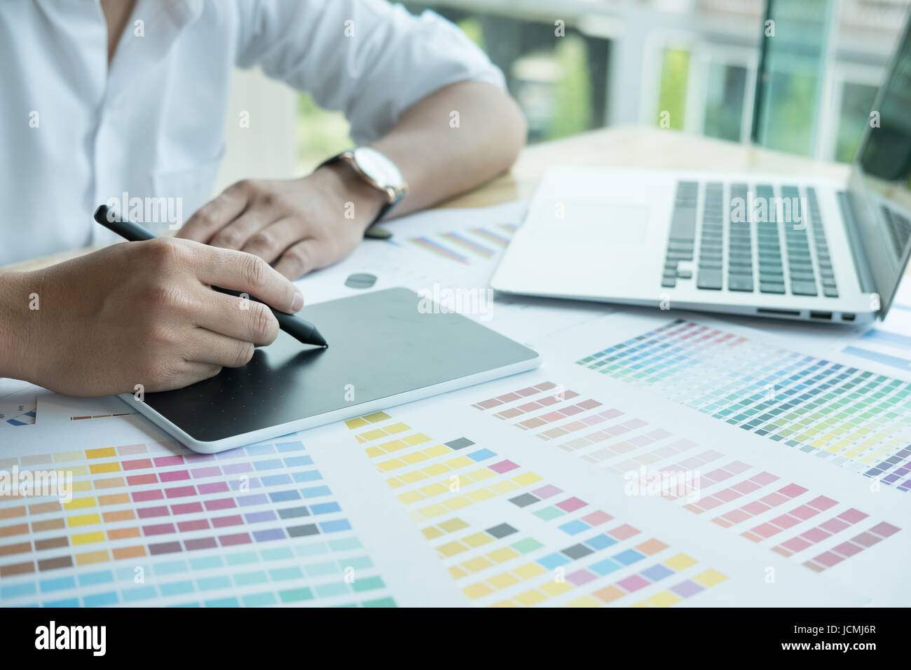 young male graphic designer working with computer and color swatch ...