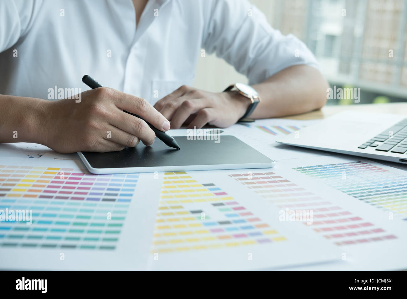 young male graphic designer working with computer and color swatch ...