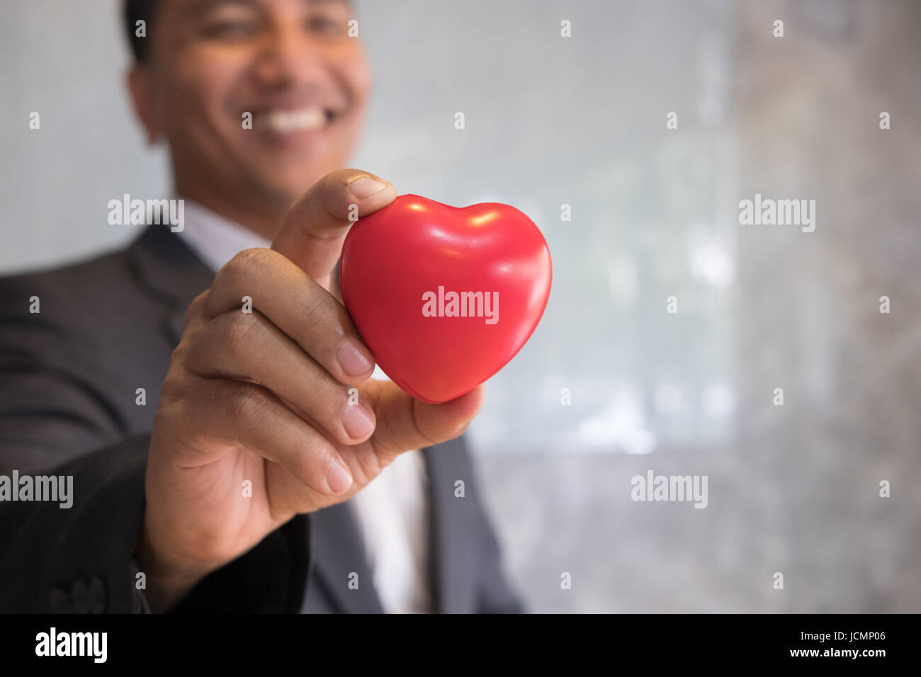 young businessman in a business suit shows big red heart at office ...
