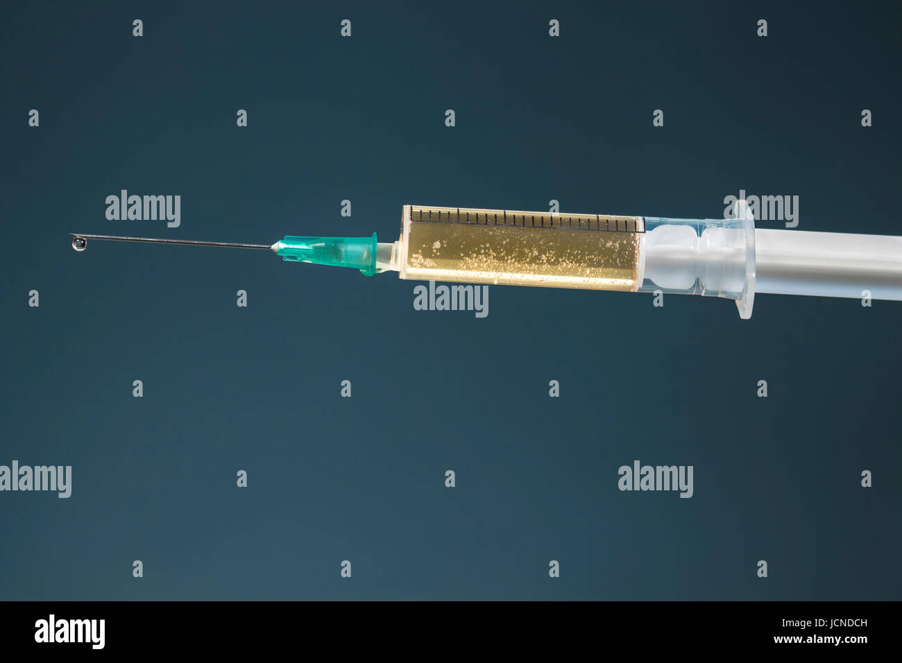 Hypodermic needle with drop at its tip and syringe with dark yellow ...