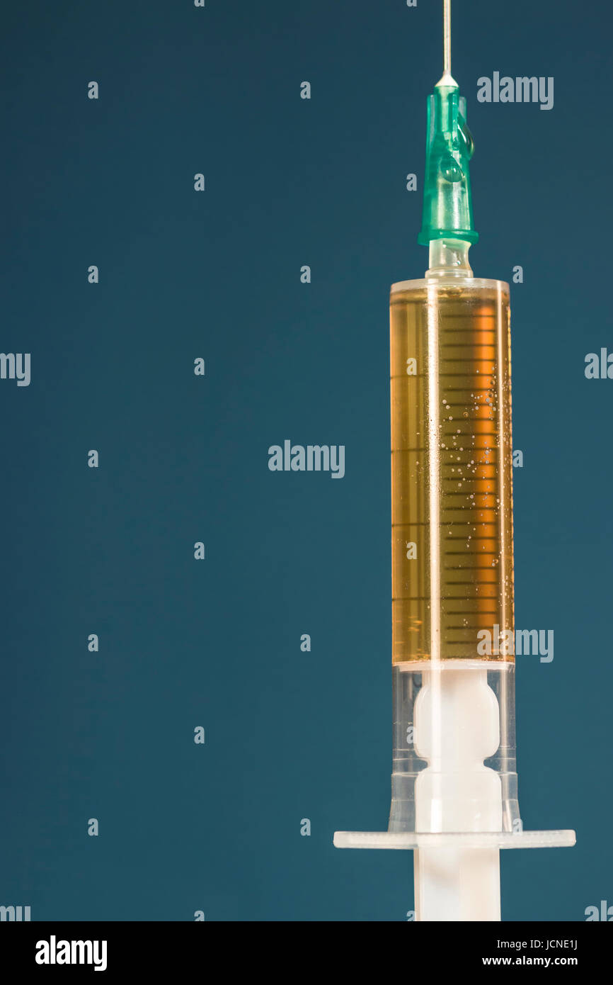 Syringe with dark yellow drug, on dark blue background and clear space ...