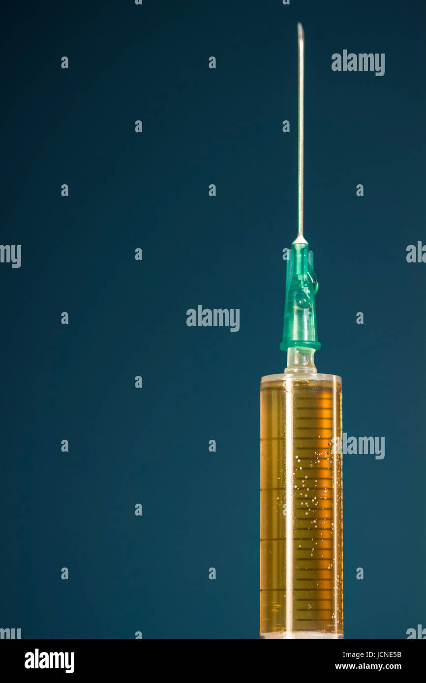 Hypodermic needle and syringe with dark yellow drug, on dark blue ...
