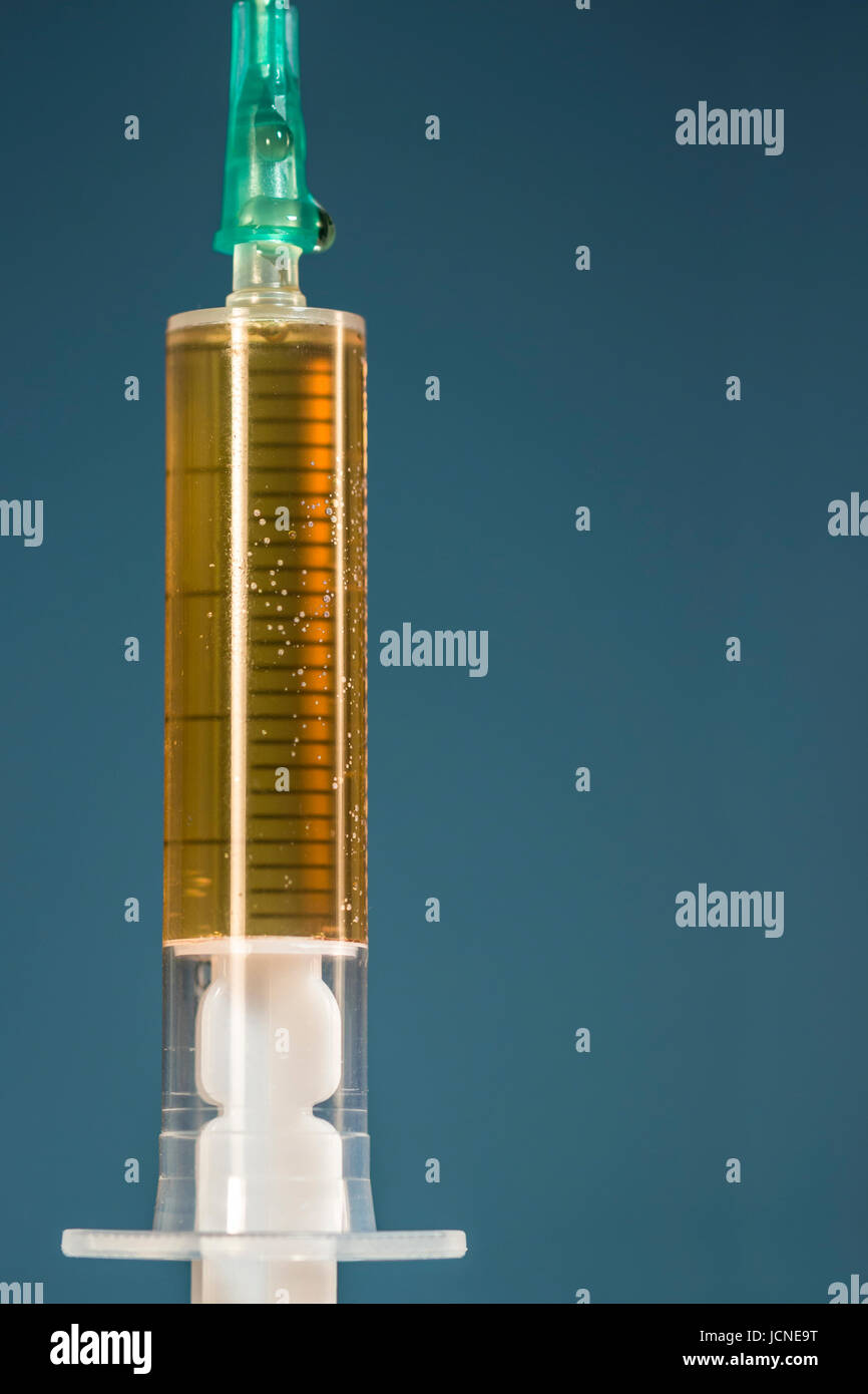 Syringe with dark yellow drug, on dark blue background and clear space ...