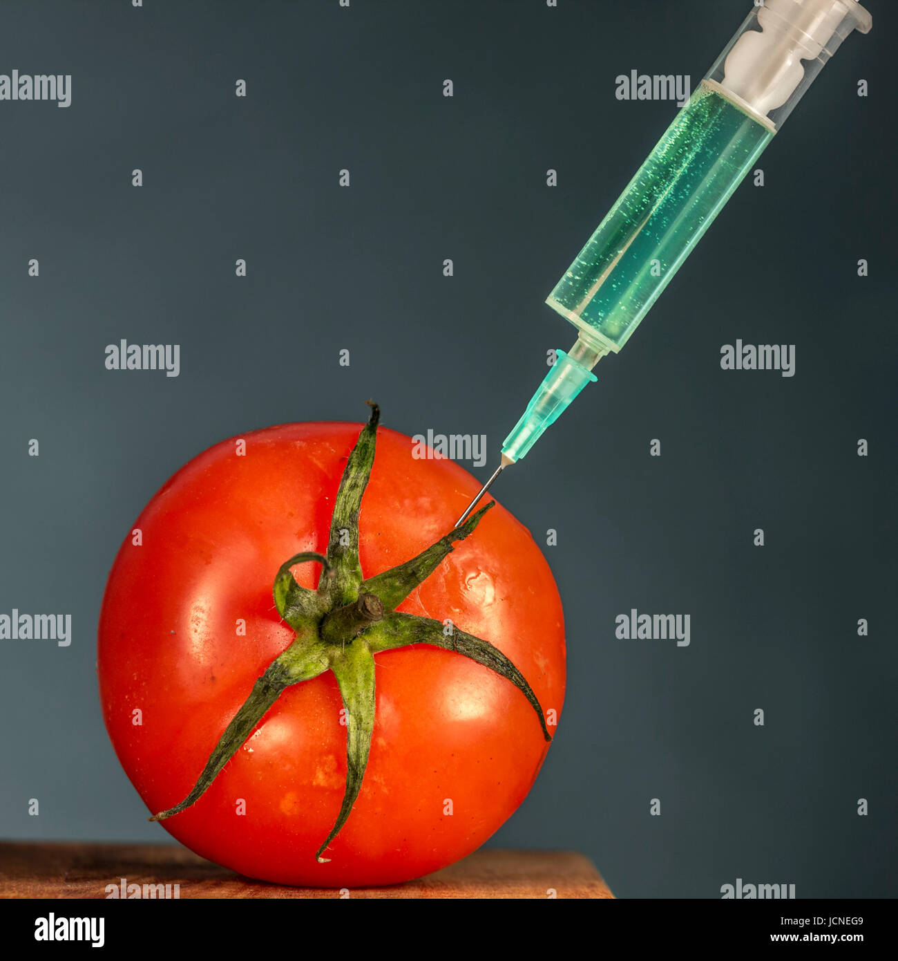 Tomato is injected a bright green substance with hypodermic needle ...