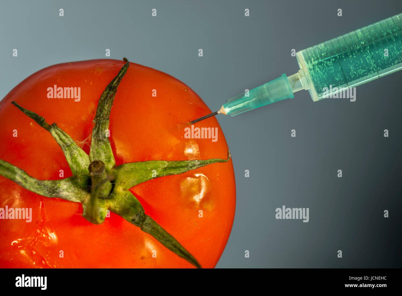 Hypodermic needle injecting a bright green substance into a red tomato ...