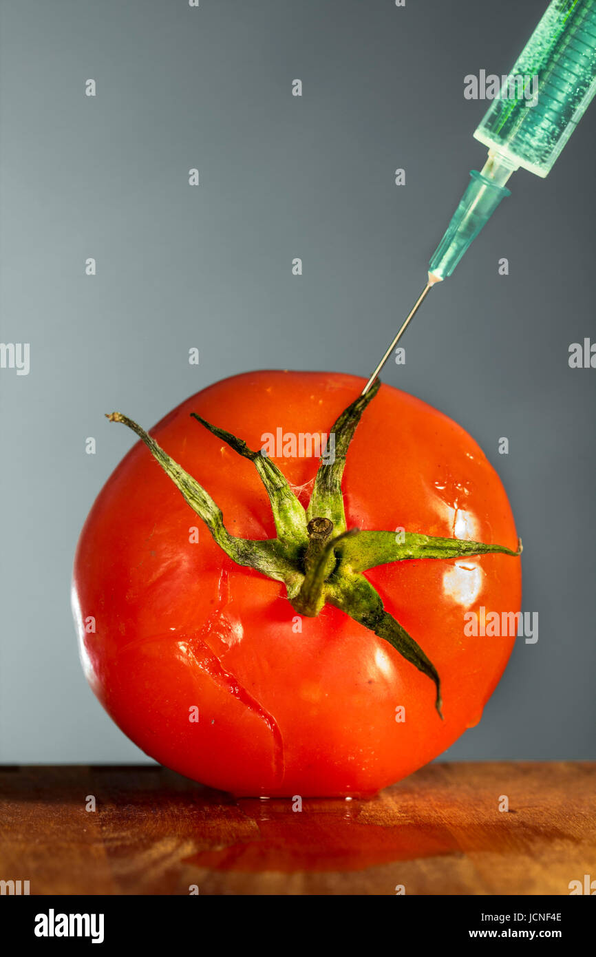 Hypodermic needle injecting a bright green substance into a red tomato ...