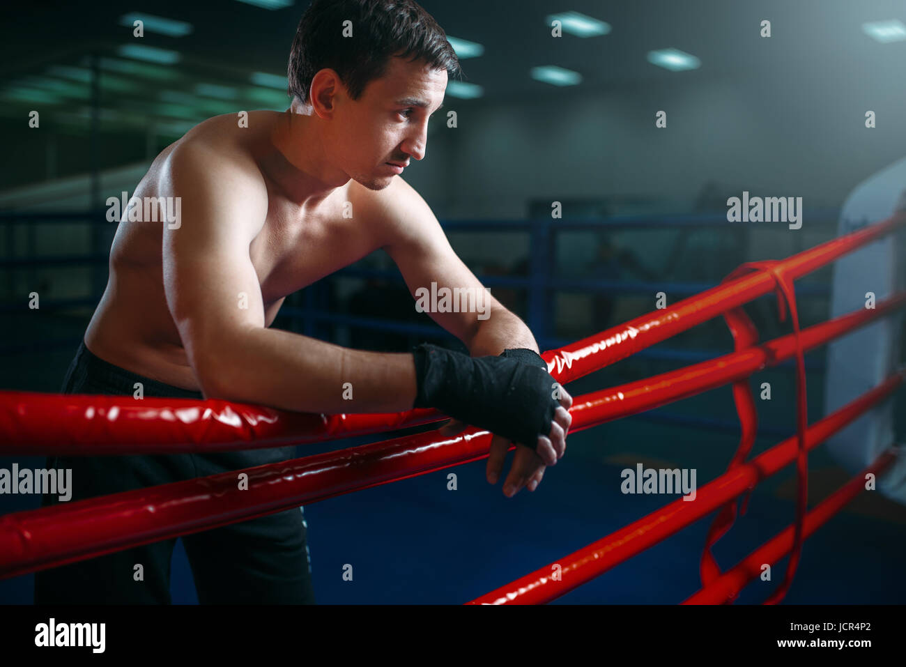 Muscular boxer in black bandages poses on the ring ropes. Boxing ...