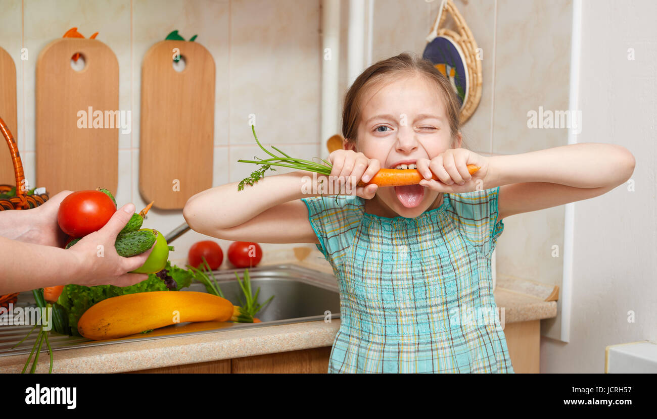 child girl eat carrot, vegetables and fresh fruits in kitchen interior ...