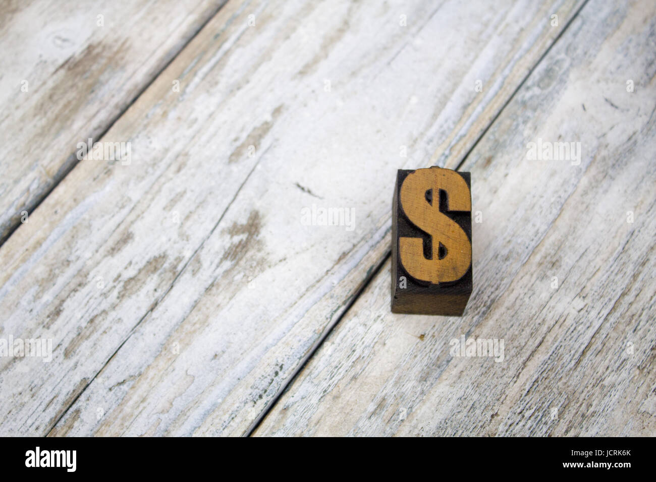 A vintage letterpress dollar sign symbol on a white washed wooden board ...