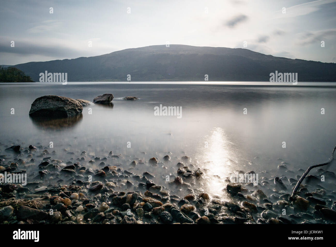 Smooth lake with rocks lit with sunlight Stock Photo - Alamy