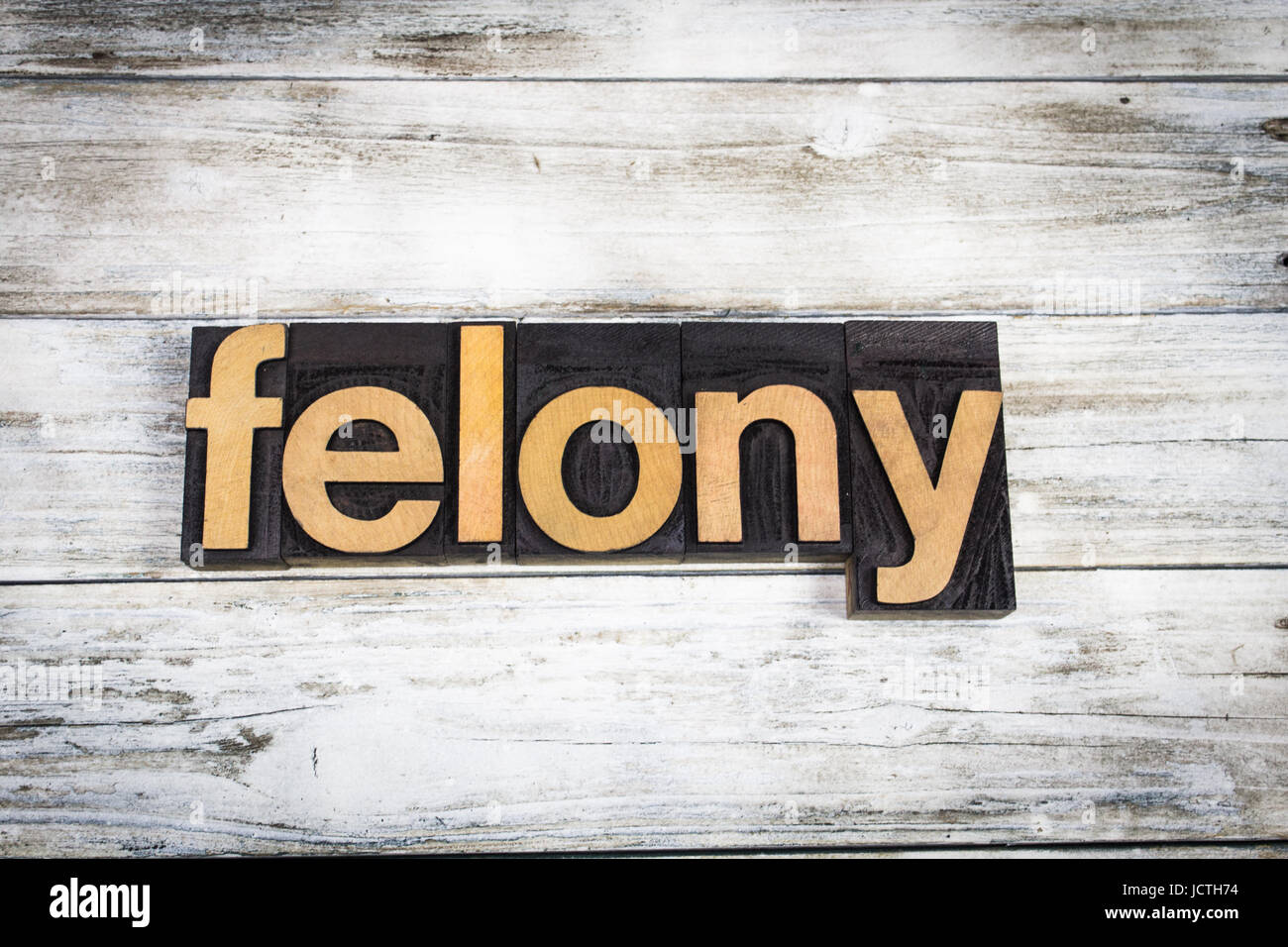 The word "felony" written in wooden letterpress type on a white washed ...