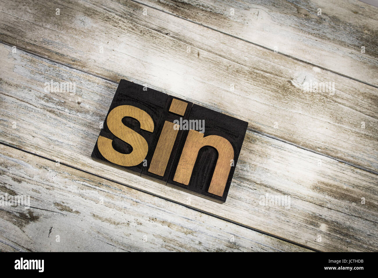 The word "Sin" written in wooden letterpress type on a white washed old ...