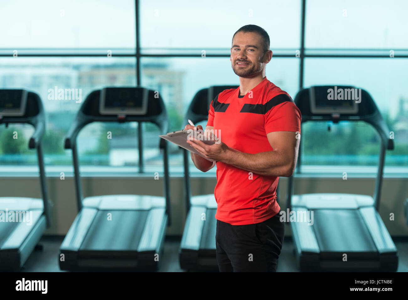 Handsome Personal Trainer With A Clipboard In The Gym And Flexing ...