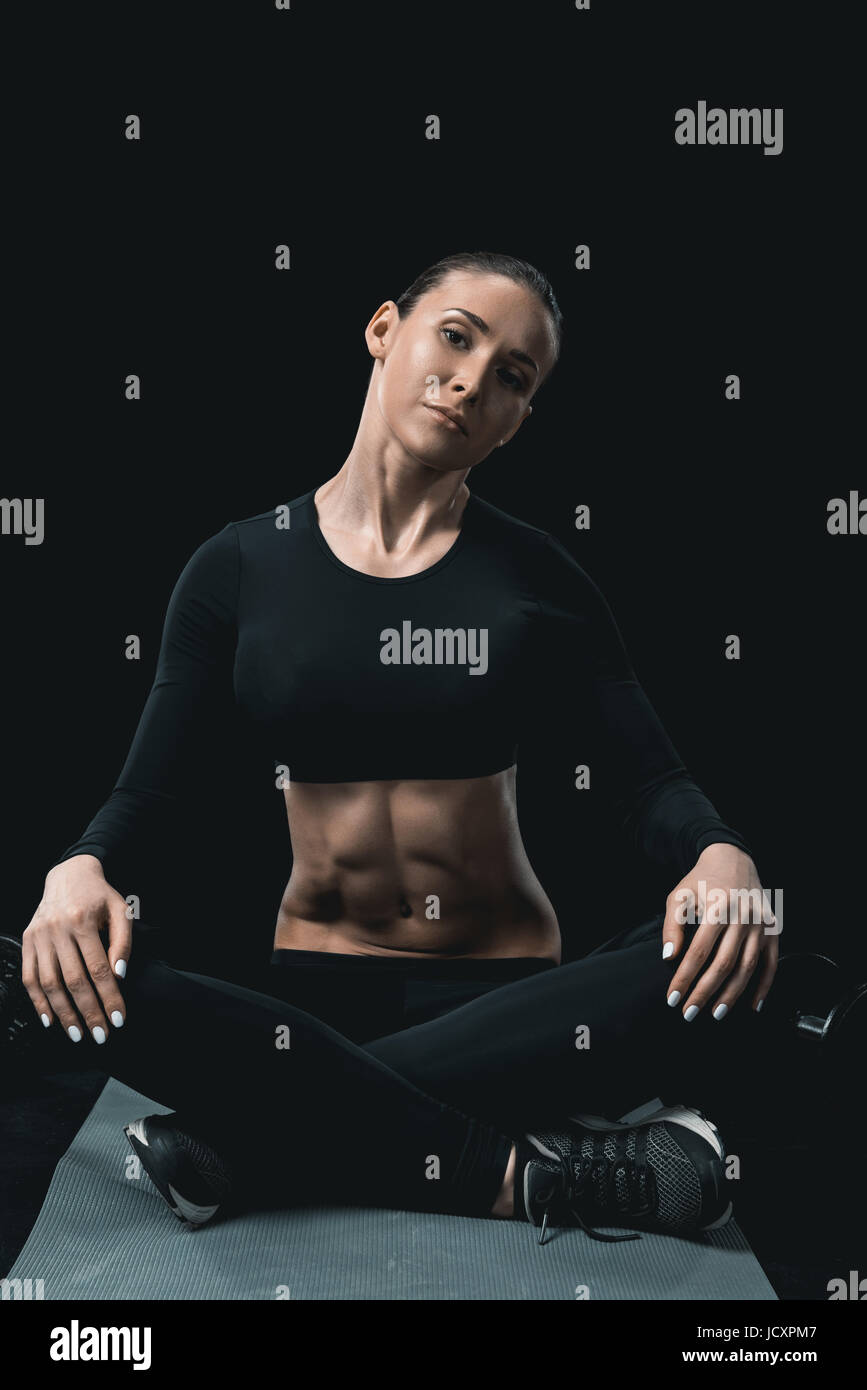 young fitness woman stretching neck while sitting on mat isolated on ...