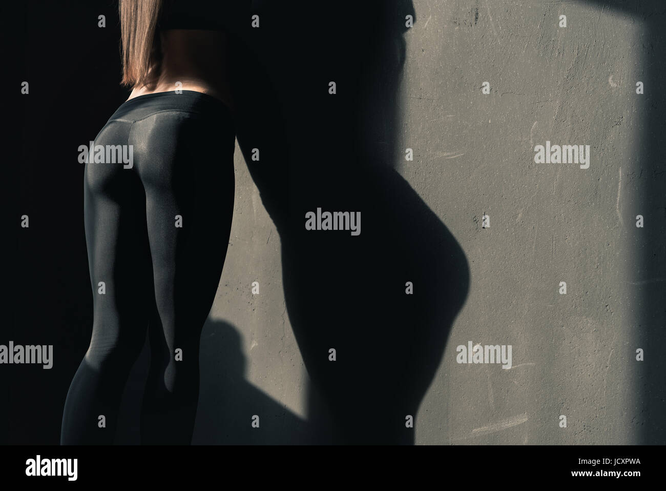 Partial back view of young fitness woman in sportswear posing on black ...