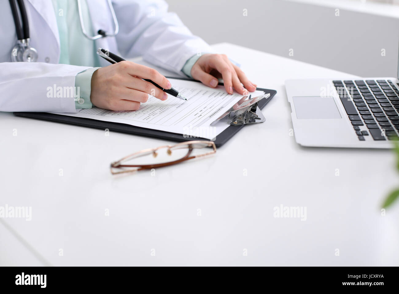Close-up of a female doctor filling out application form , sitting at ...