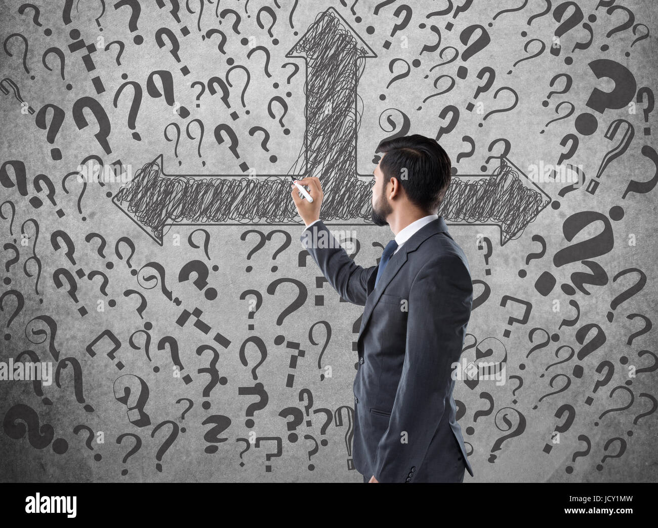 Businessman drawing arrow directional sign with question marks on wall ...