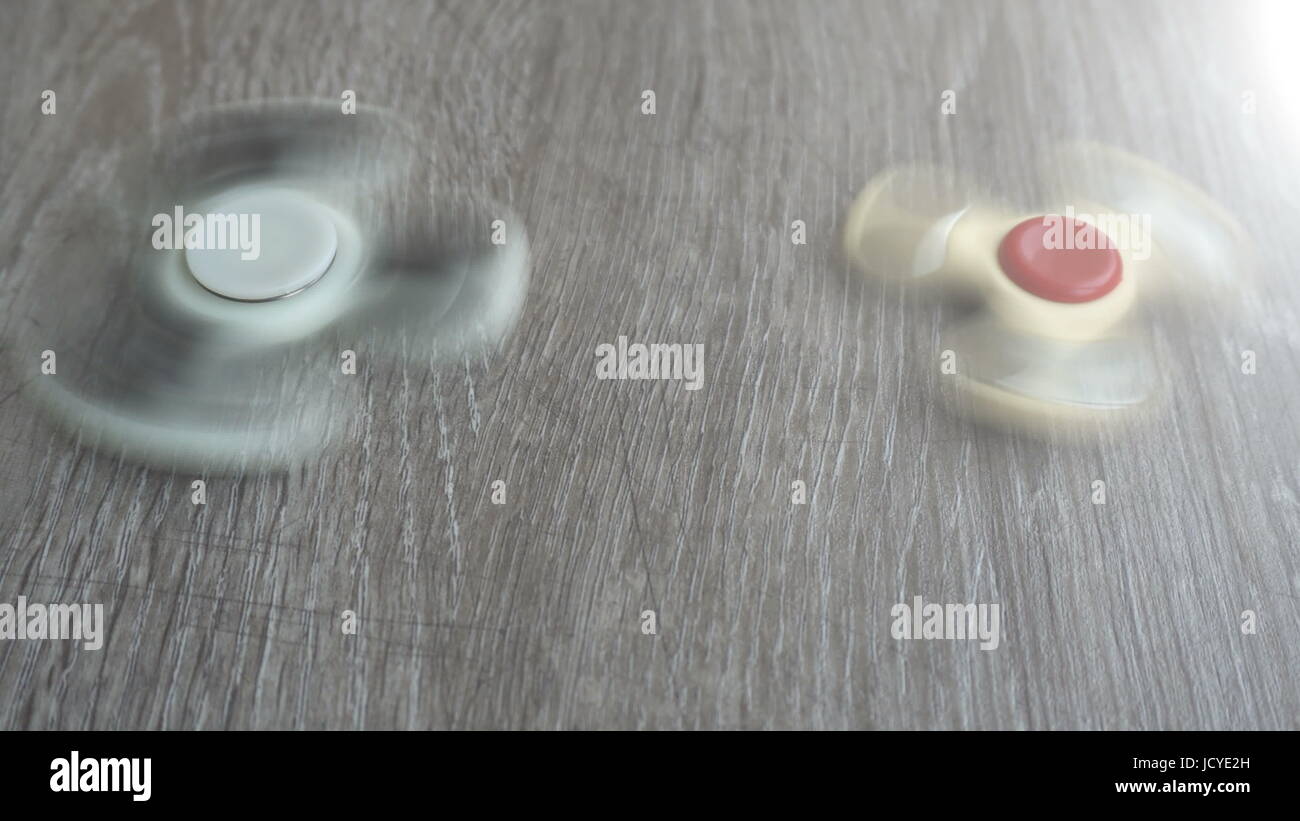 two white hand spinner spinning on grey background or fidget spinners ...