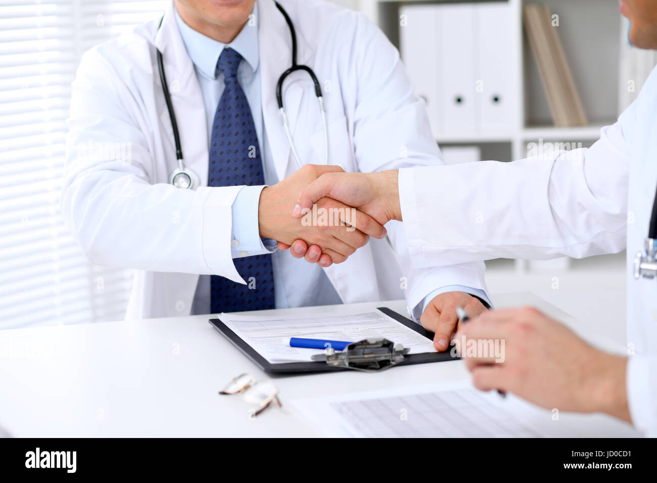 Two doctors shaking hands to each other sitting at the table in ...