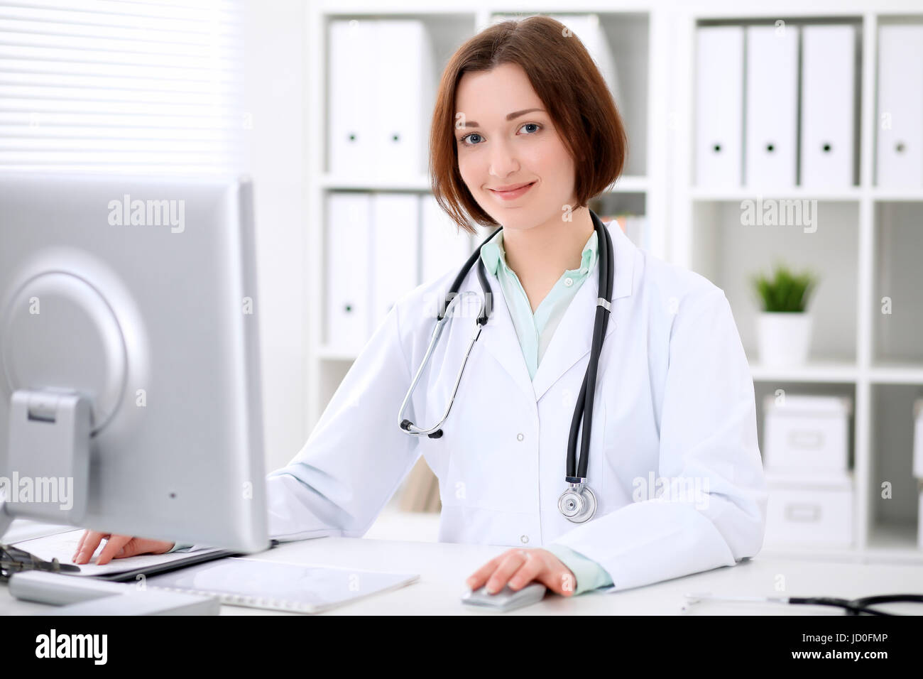 Young brunette female doctor sitting at a desk and working on the ...