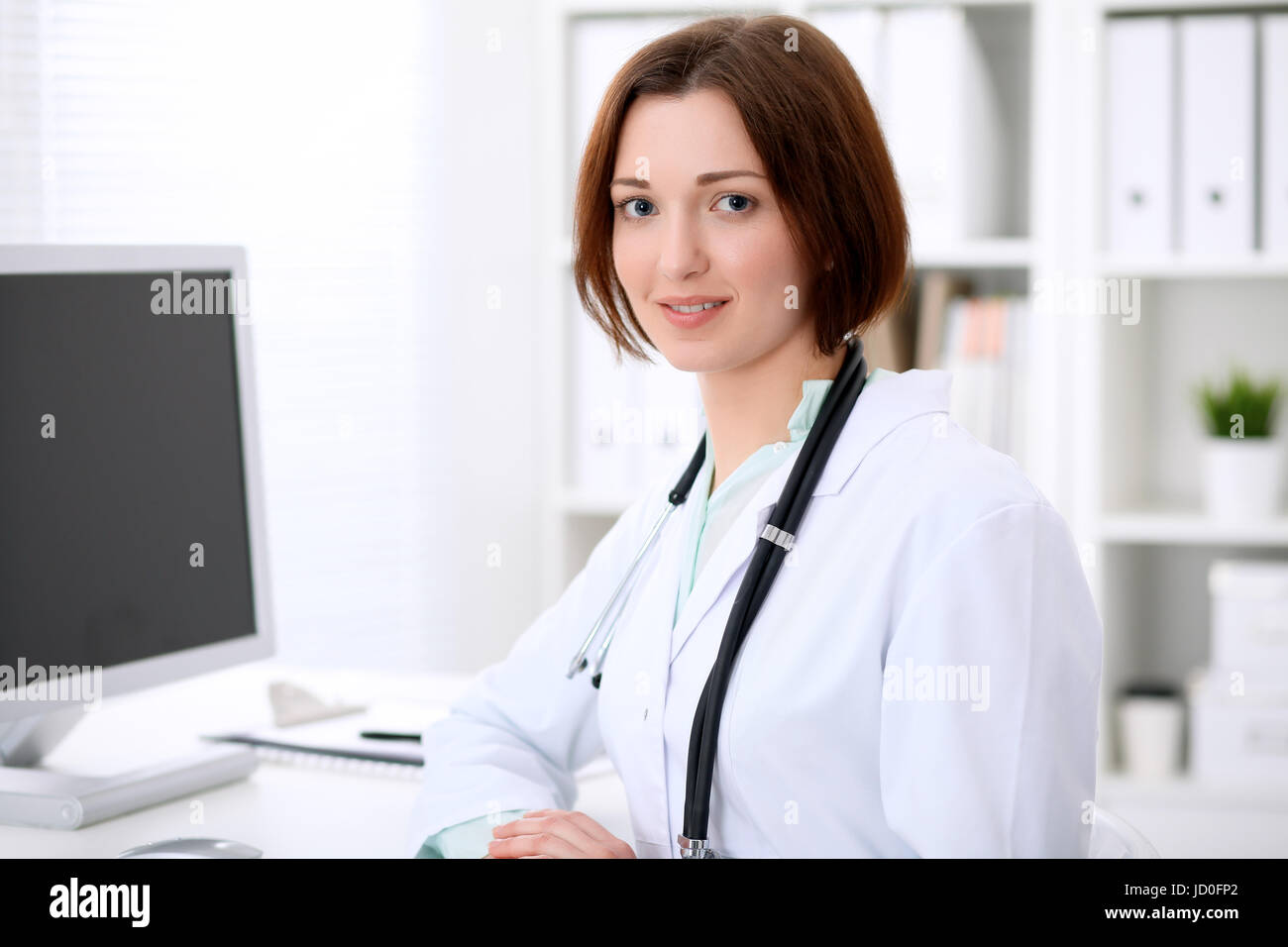 Young brunette female doctor sitting at a desk and working on the ...