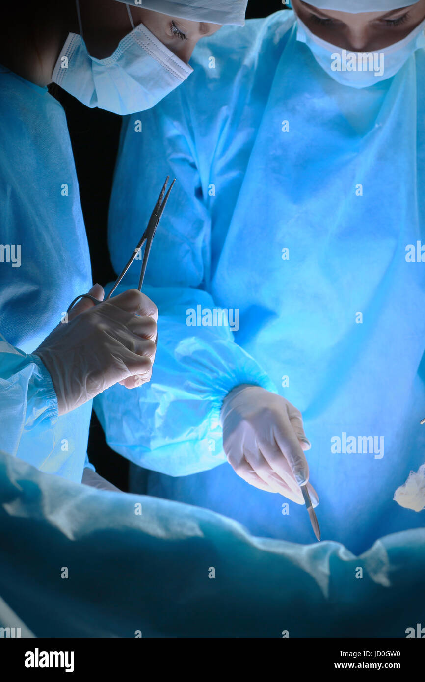Group of surgeons at work in operating theater toned in blue. Medical ...