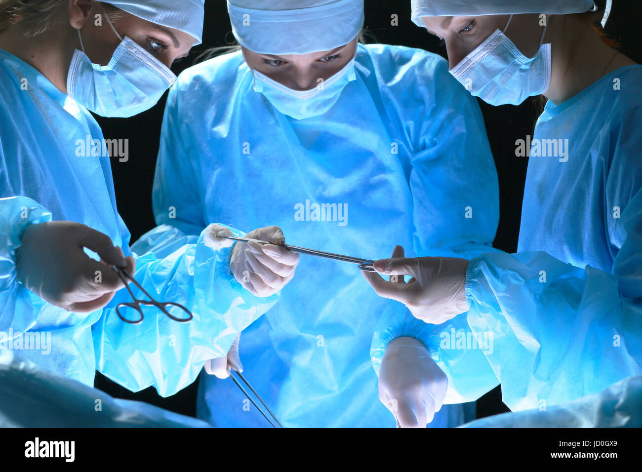 Group of surgeons at work in operating theater toned in blue. Medical ...
