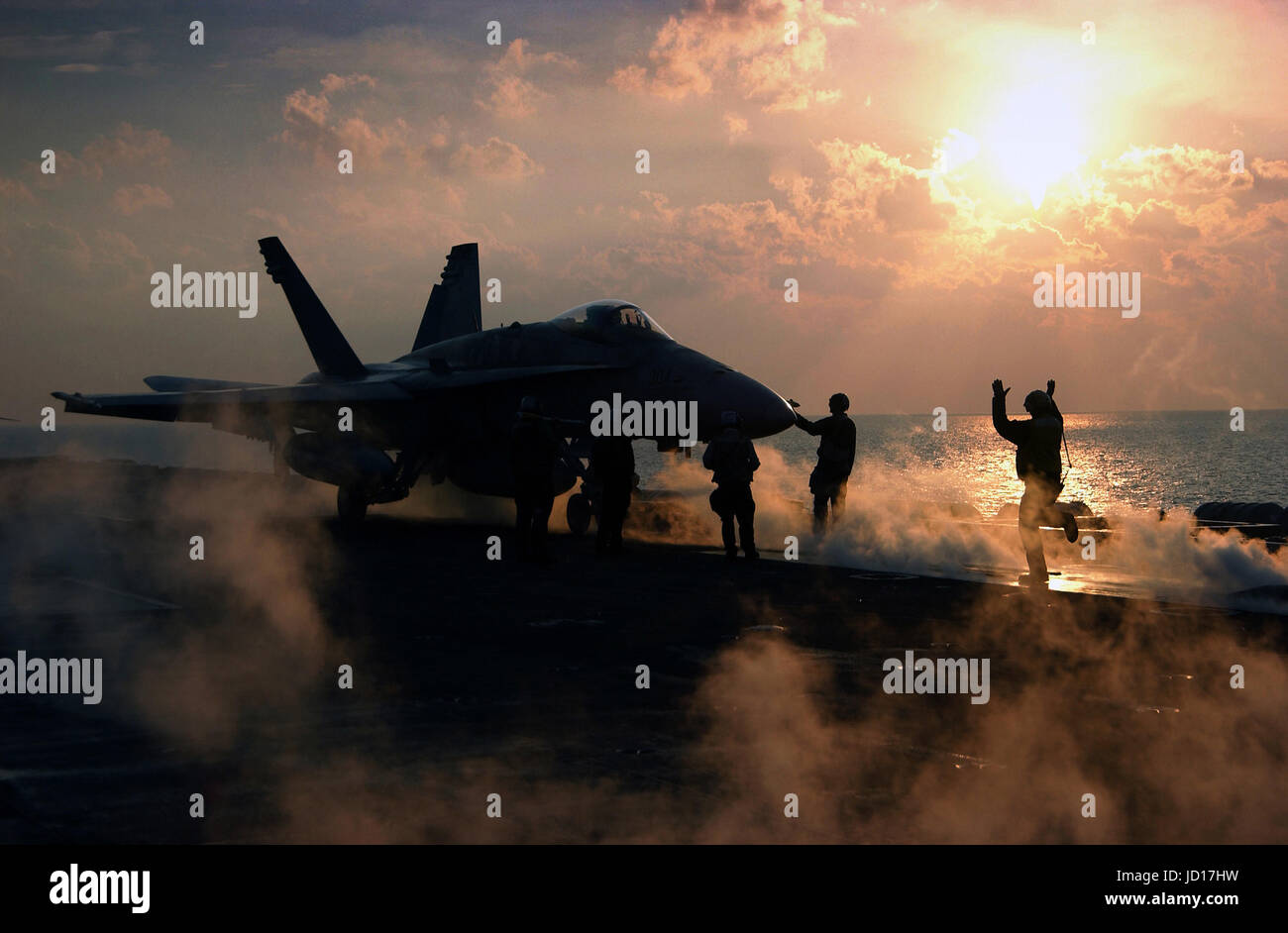 A U.S. Navy flight deck handler guides an F/A-18 Hornet aircraft into ...