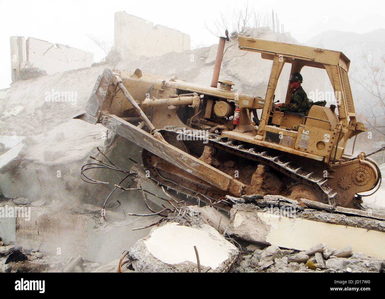A U.S. Navy Seabee operates a bulldozer to demolish an unsafe building ...
