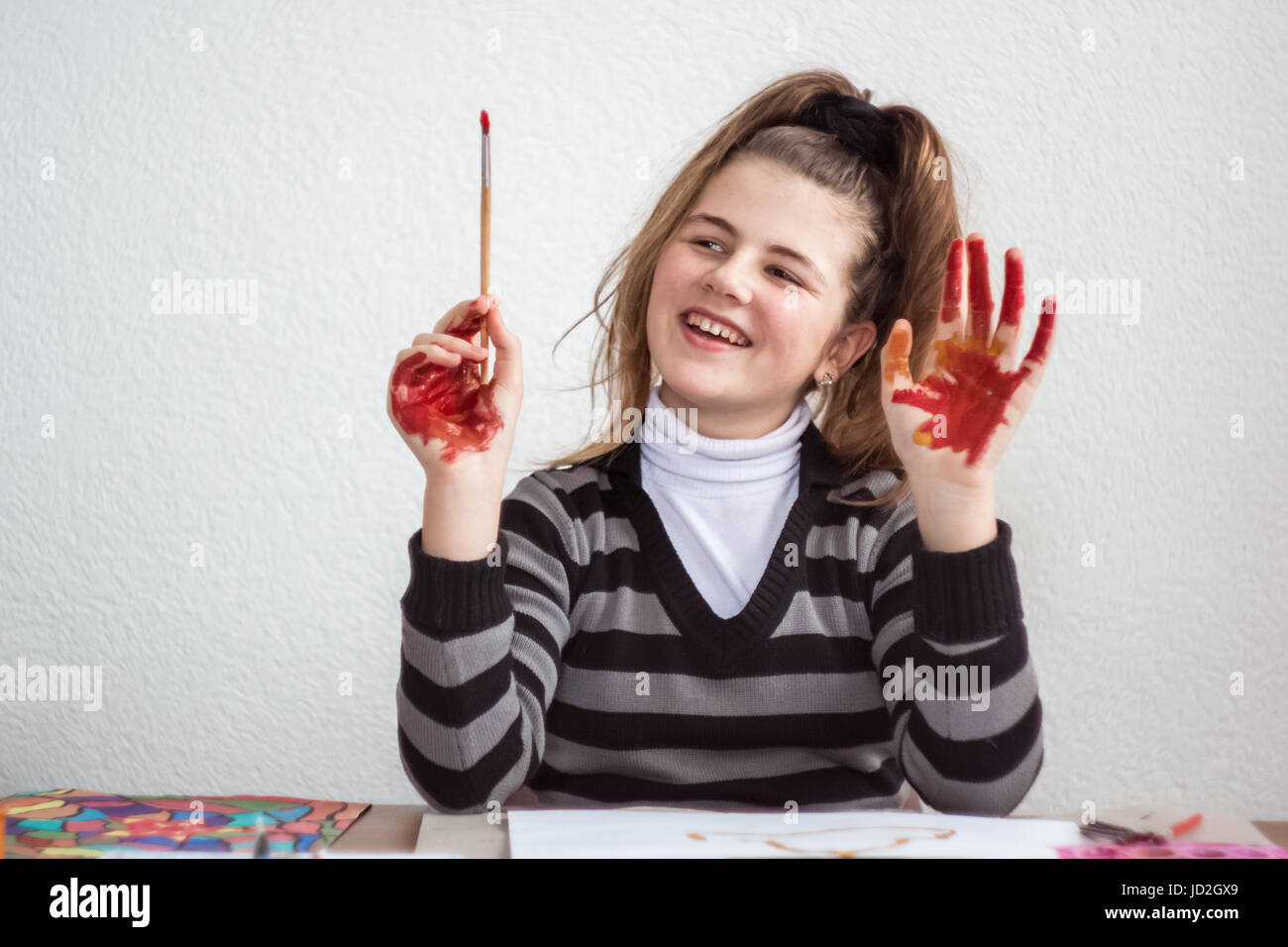 Girl painting with brush and colorful paint and smeared hands of colors ...