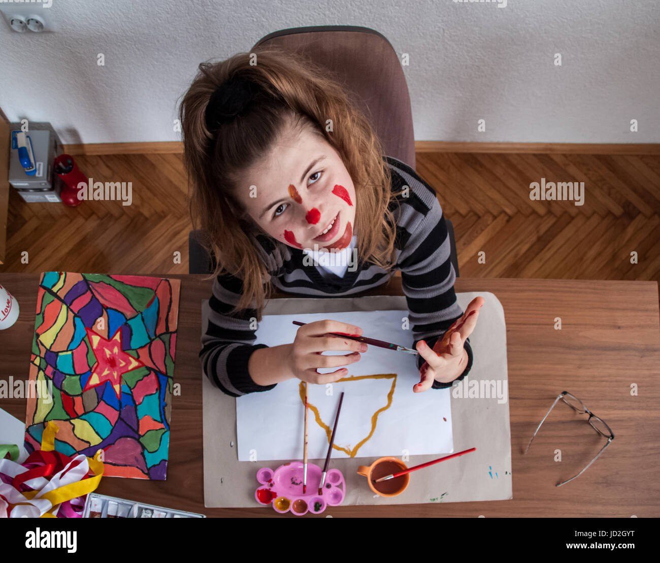 Girl painting with brush and colorful paint with smeared face and hands ...