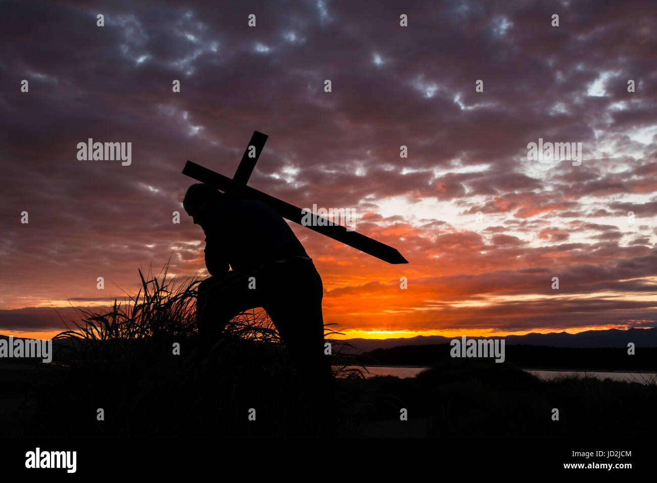 Man carrying a cross up a hill at sunrise Stock Photo - Alamy