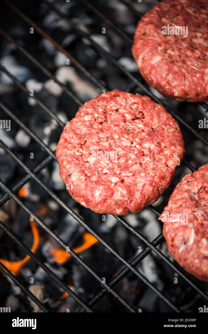 Raw burgers on bbq grill with flames Stock Photo - Alamy