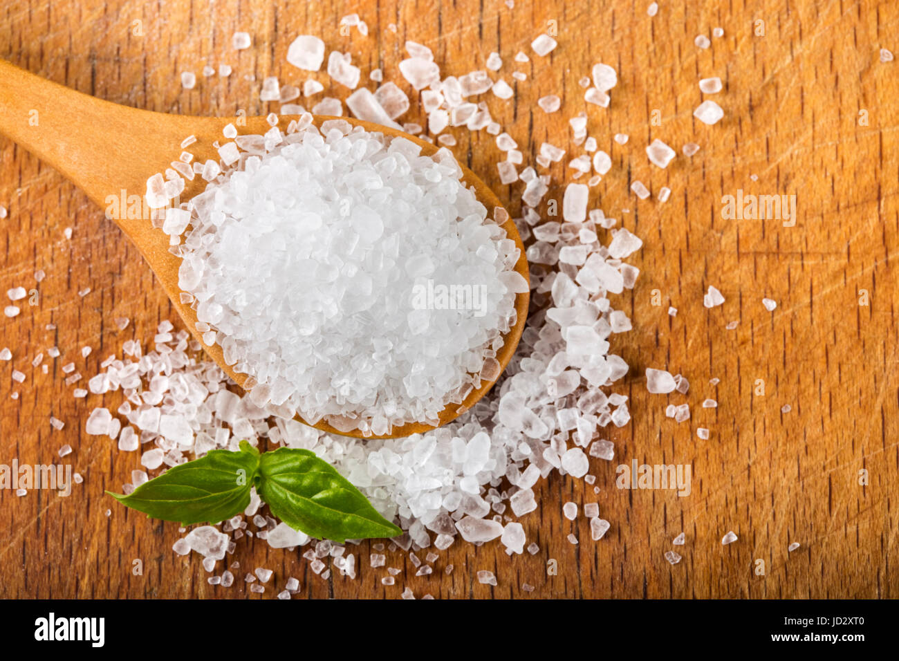 Sea salt in wooden spoon with basil leaf over wood background Stock ...