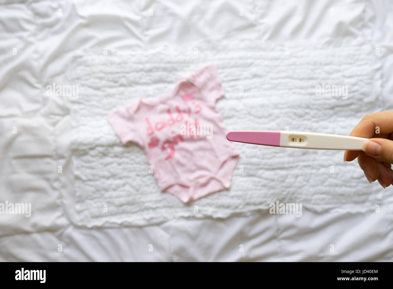 Positive pregnancy test in woman hand and baby clothes on white ...