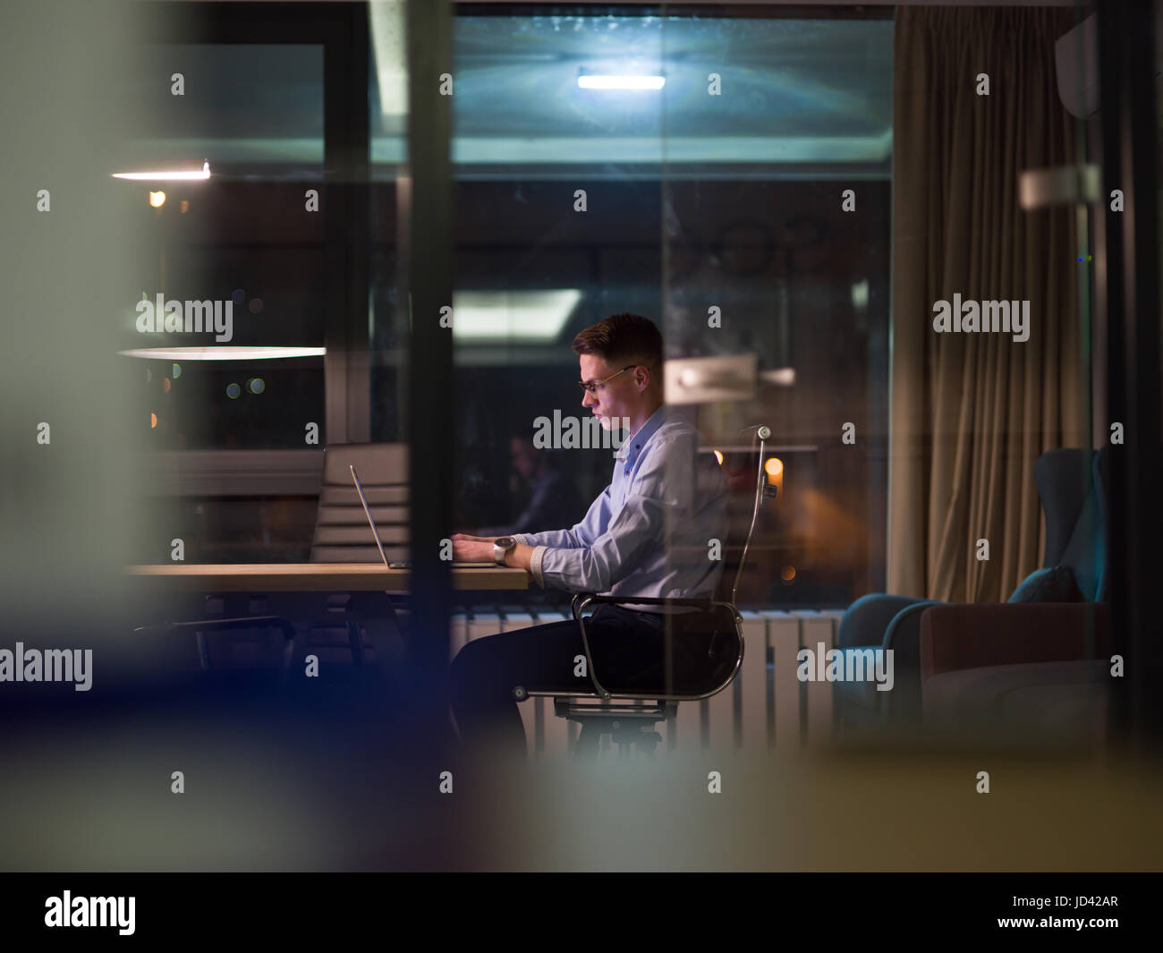 Young man working on laptop at night in dark office. The designer works ...