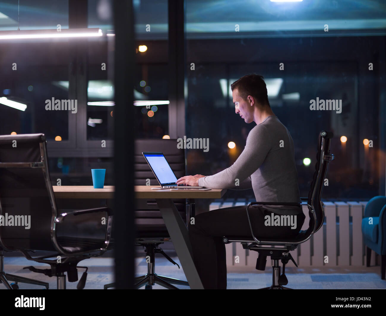 Young man working on laptop at night in dark office. The designer works ...
