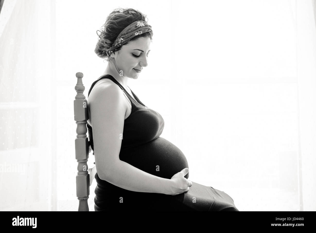 Pretty young pregnant woman sitting by the window in room Stock Photo ...