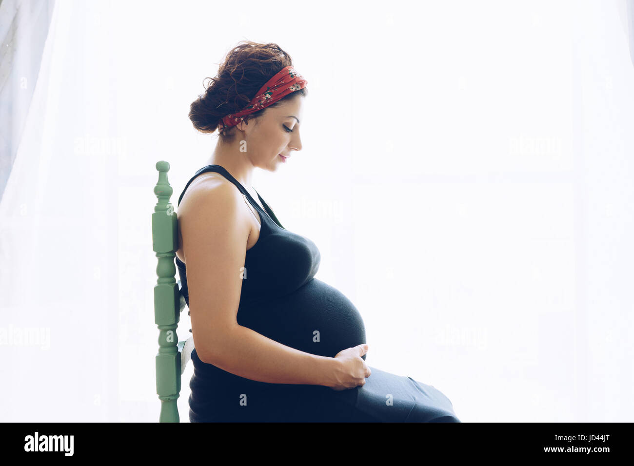 Pretty young pregnant woman sitting by the window in room Stock Photo ...