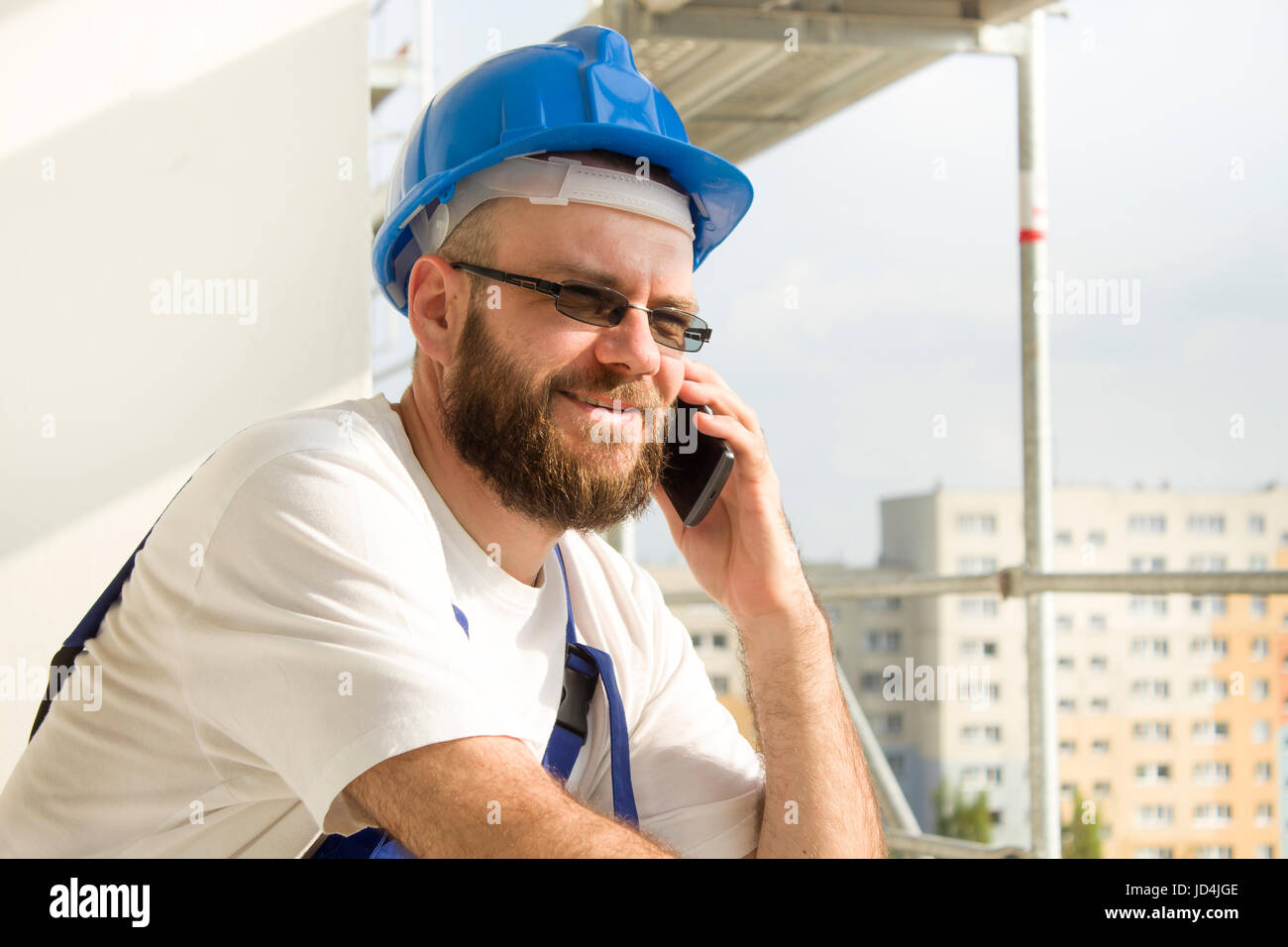 Smiling construction worker in work outfit and helmet on head talking ...