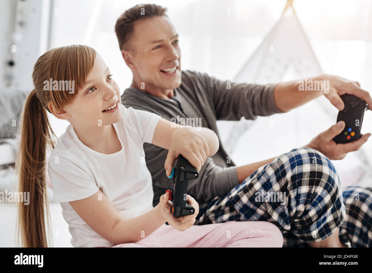 Engaged emotional child and her father using controllers for playing ...